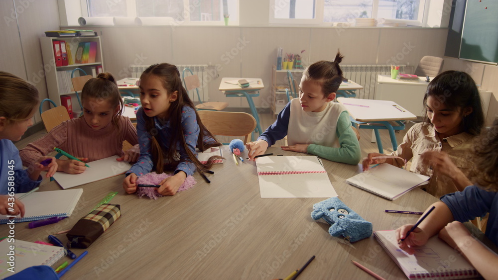 Students talking during lesson at round desk. Cheerful kids having ...