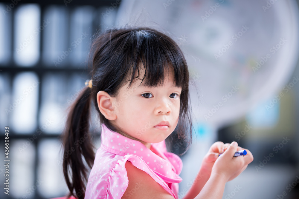 A 4 year old Asian girl is holding a blue crayon in her hand. Child is ...