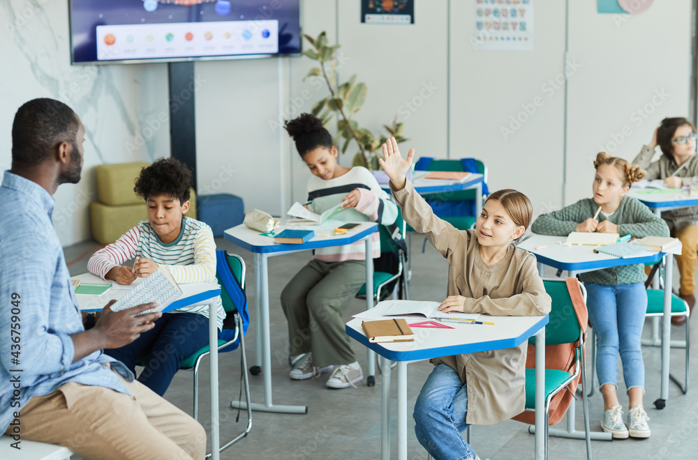 Diverse group of children in school classroom with smiling girl raising ...