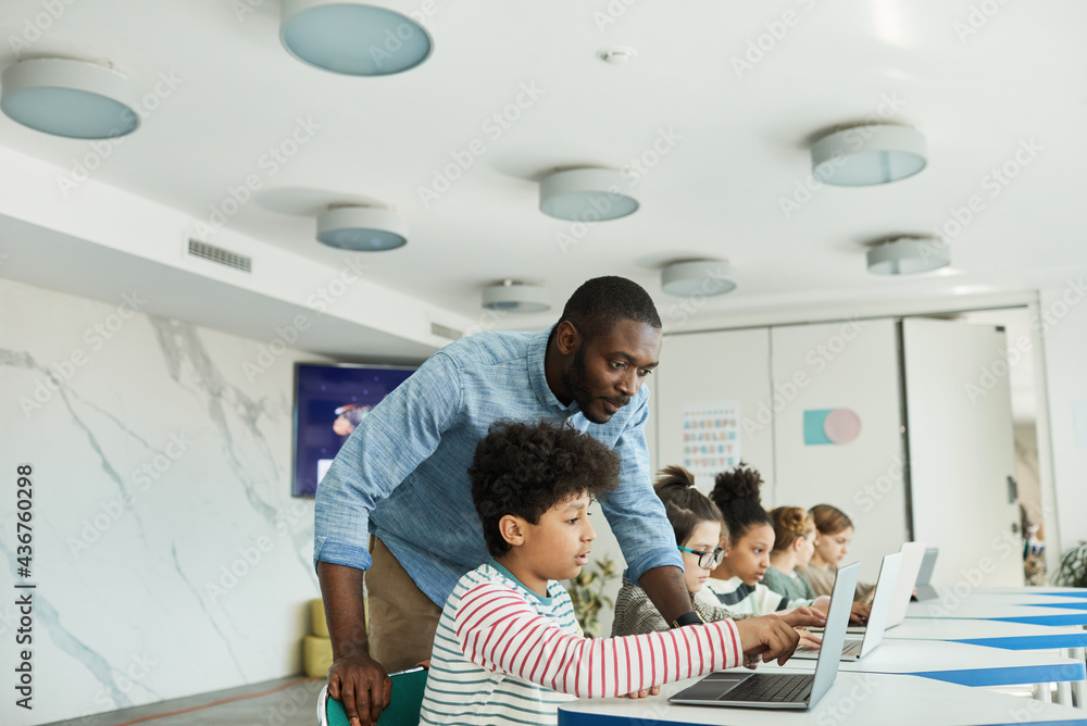 Wide angle side view portrait of young boy using computer in IT class ...