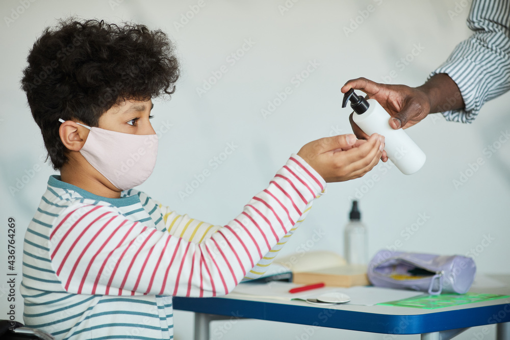 Side view portrait of boy wearing mask and sanitizing hands in school ...