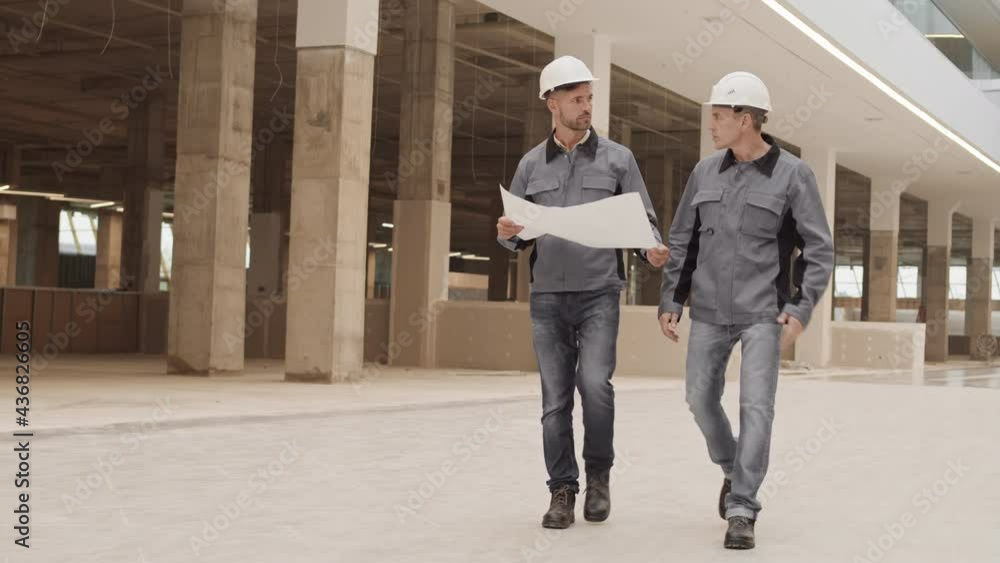 Wide tracking of two male Caucasian builders wearing white hard hats ...