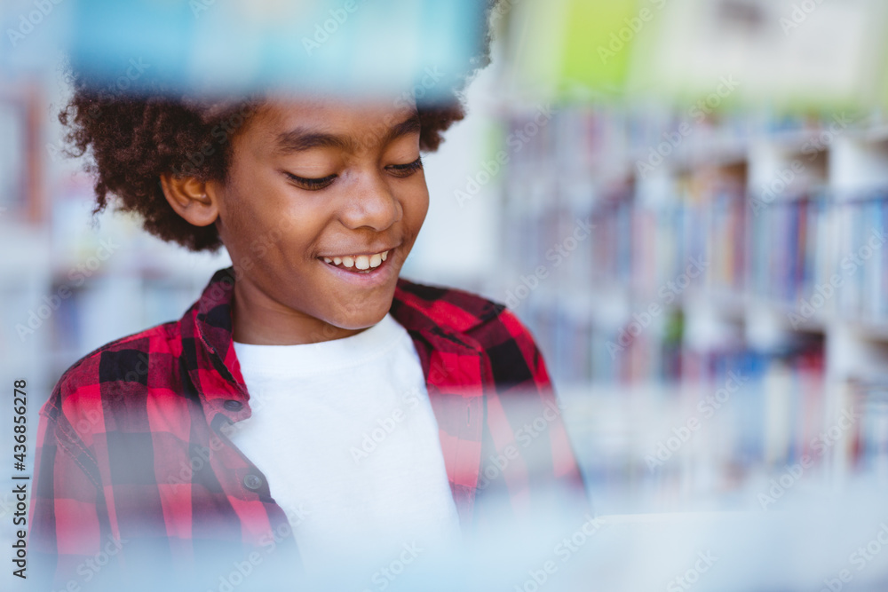 Laughing african american schoolboy reading book standing in school ...