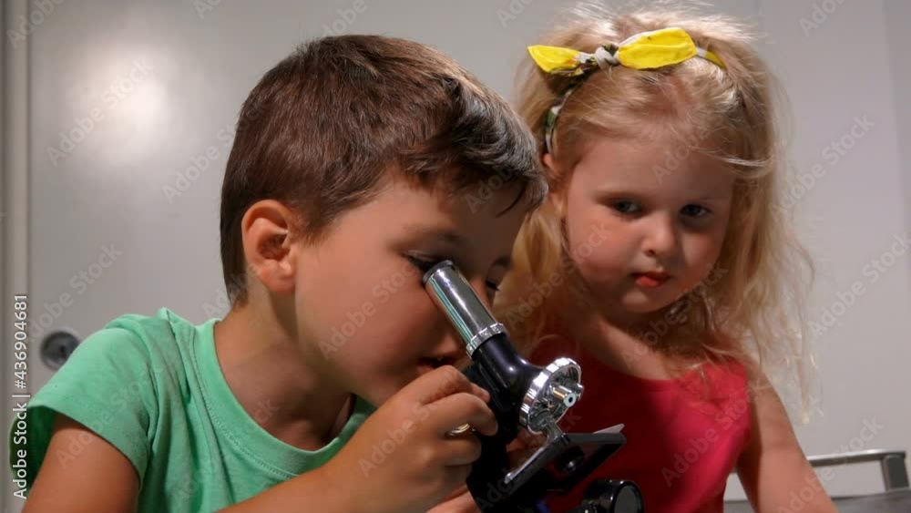 Llittle boy is sharing a microscope with a cute little girl in a white ...