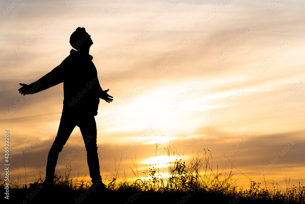 chico joven con brazos abiertos y cabeza alta, a contra luz atardecer ...