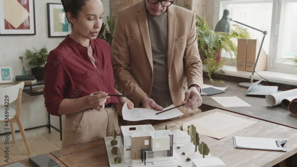 Tilt-up medium slowmo of couple of professional architects examining ...