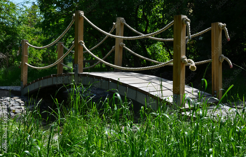 arched wooden bridge in the park. the railing posts are connected by a ...