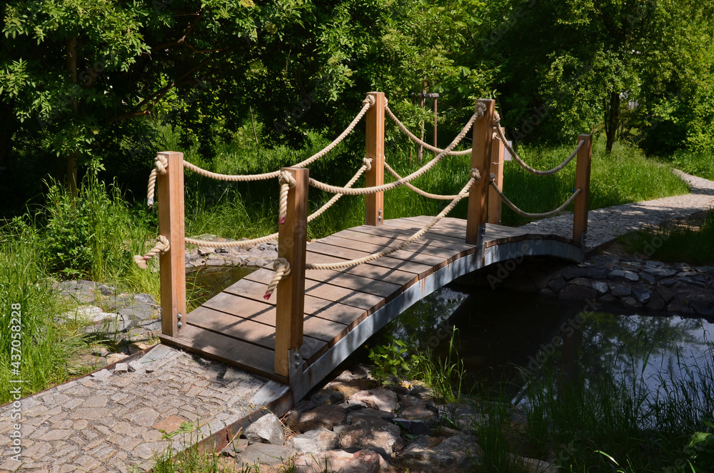 arched wooden bridge in the park. the railing posts are connected by a ...