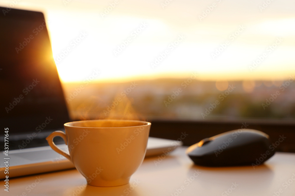 Hot coffee cup and laptop on table against the window at sunset. Cozy ...