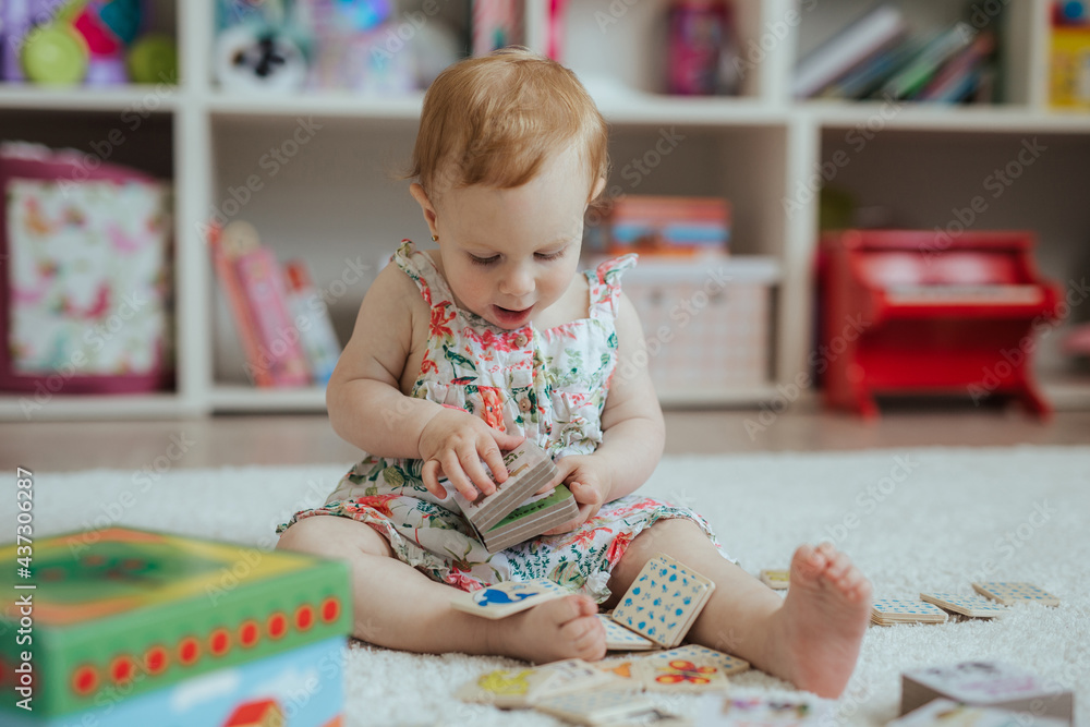 Little curious baby girl playing on a playground in a bright sunny room ...