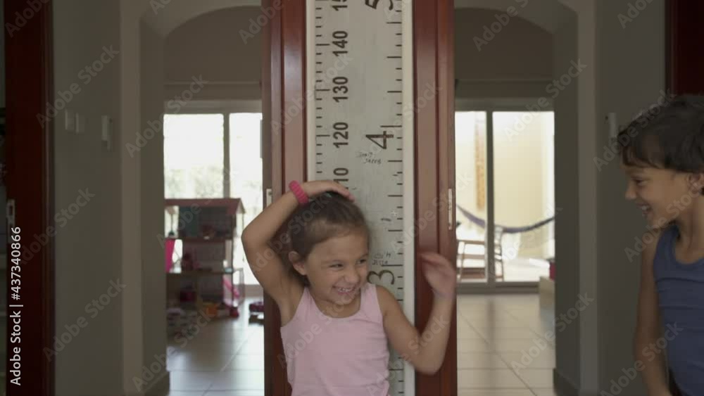 Little girl measuring her height and fighting with her brother for a ...