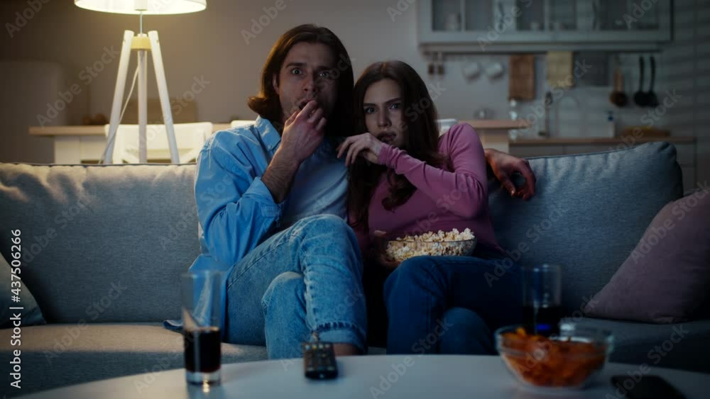 Scary movie night. Young frightened couple sitting on couch with ...