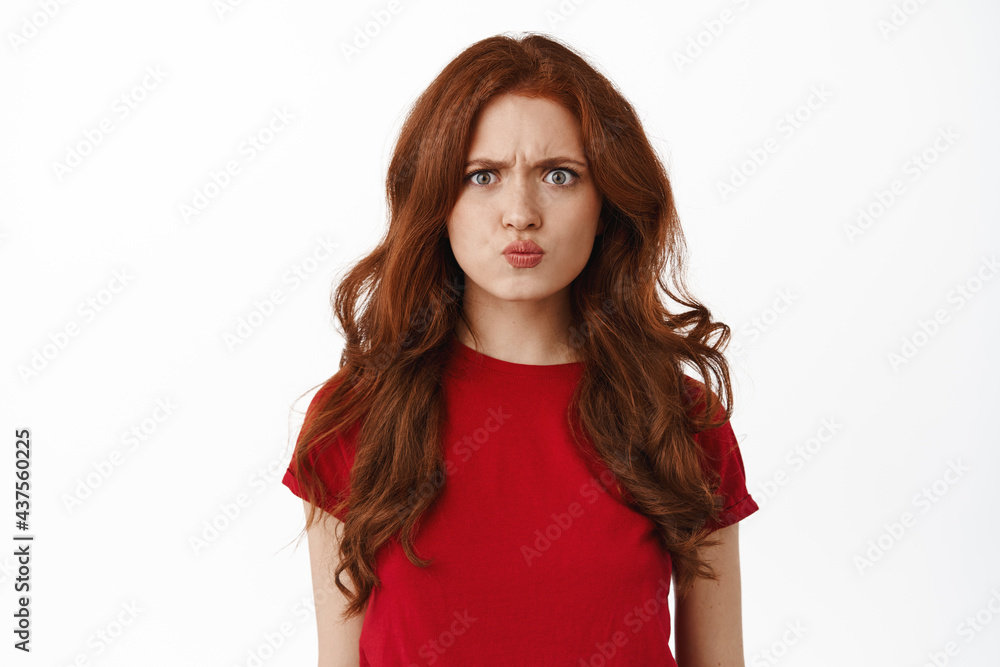 Confused and angry redhead girl pouting, frowning and grimacing ...