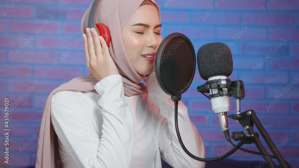 Young smiling muslim female singer wearing headphones with a microphone ...