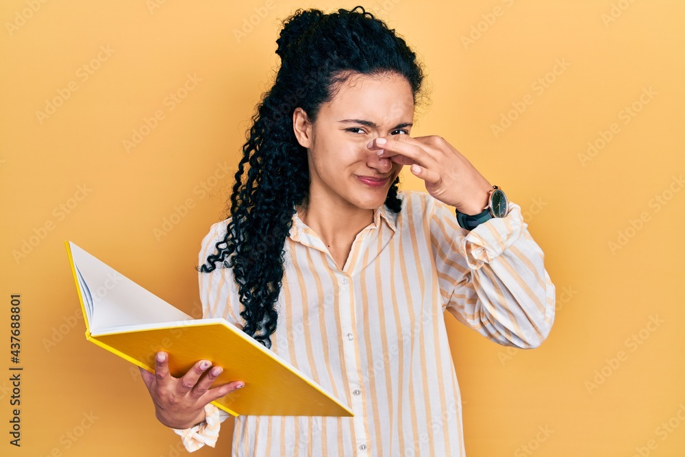Young hispanic woman with curly hair holding book smelling something ...