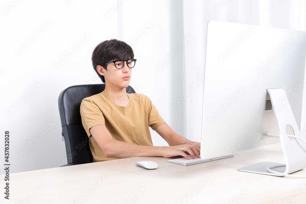 Serious teenage boy sitting on the chair while using computer at home ...