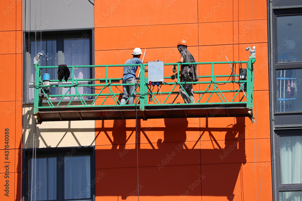 Worker standing on lifting platform near the wall of high-rise house ...