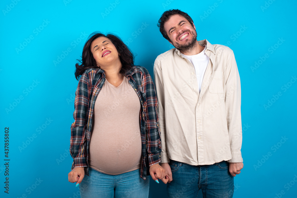 Positive young couple expecting a baby standing against blue background ...