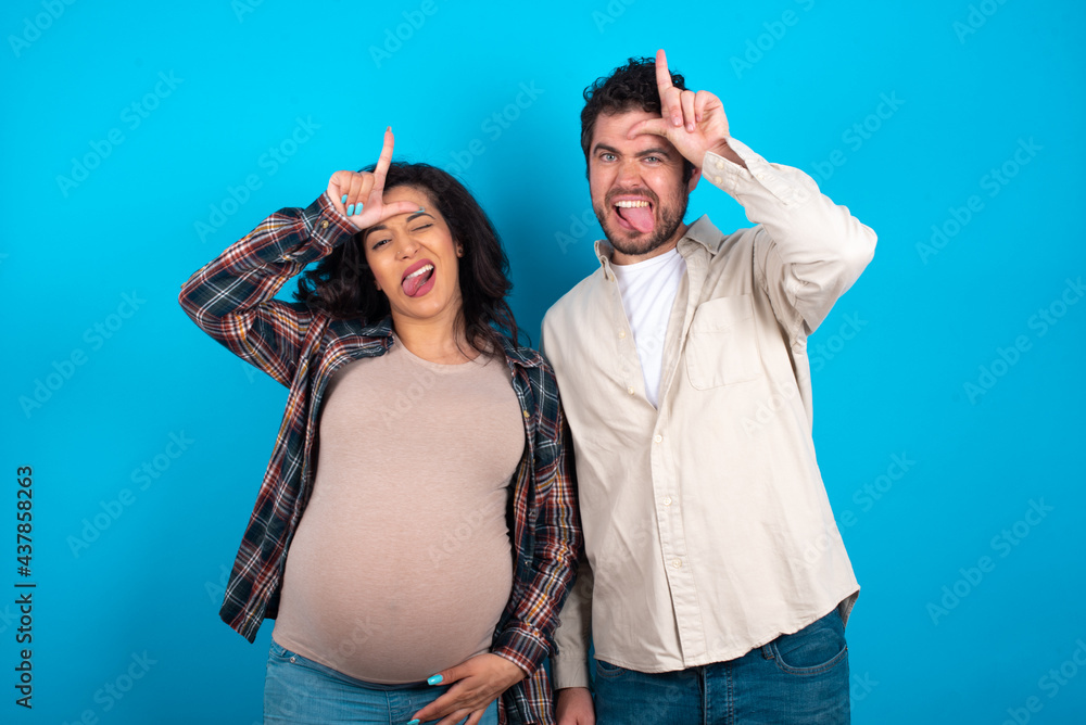 Funny young couple expecting a baby standing against blue background ...