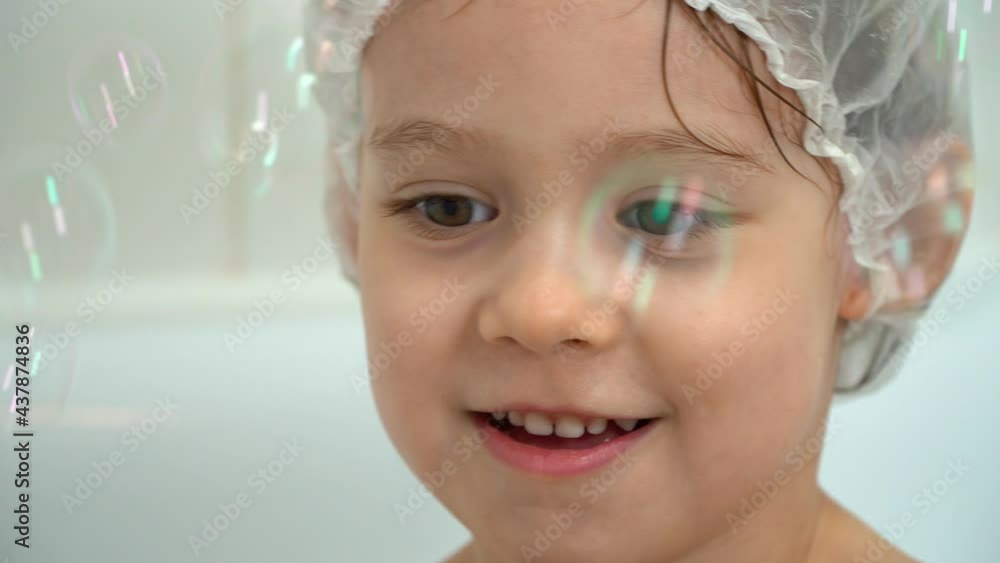 Close up of little girl catches bubbles with hands in bath, smiles and laughs. Happy child ...