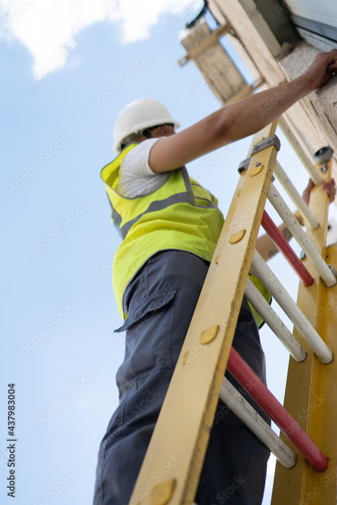 telecommunications technician working at the top of a ladder wearing ...
