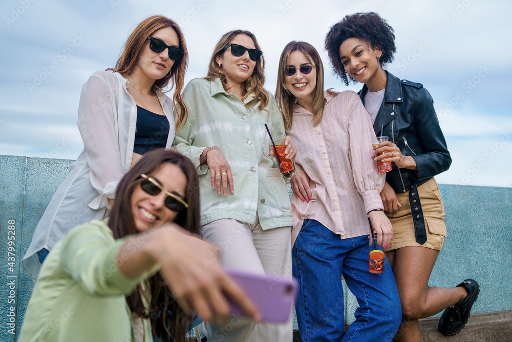 Multiracial group of female friends taking selfies on the street. They ...