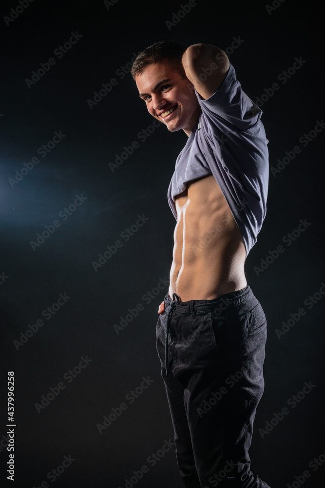 Sexy male model showing his abs while posing in a studio on dark ...