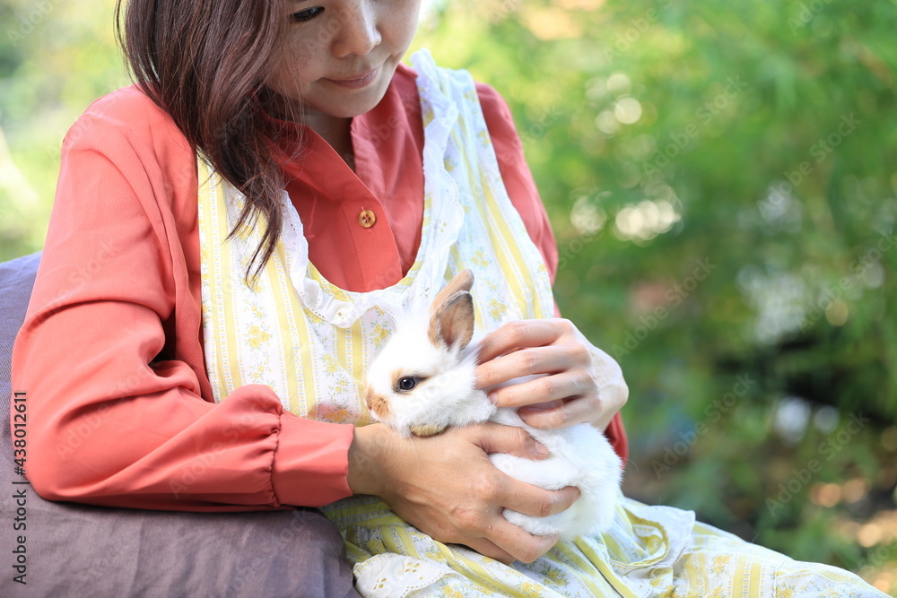 Adorable young rabbit and woman sit together outdoor. Owner care little ...