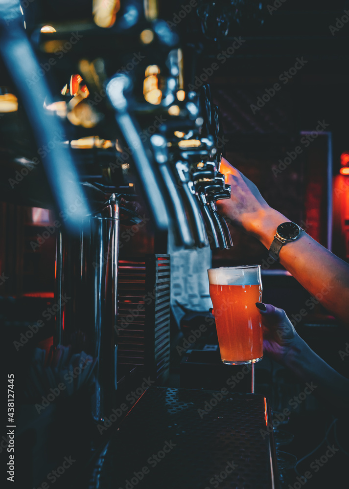 bartender hand at beer tap pouring a draught beer in glass serving in a ...