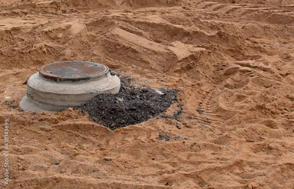 Cast-iron sewer hatch on a concrete base, located on mound of damp soil ...