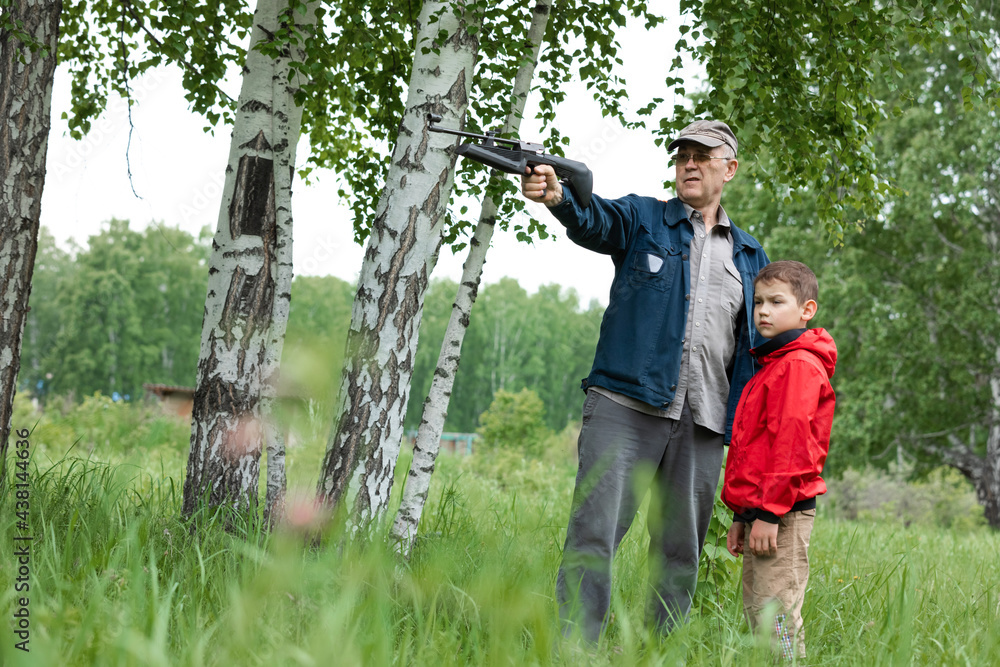 A boy in a red windbreaker with a grandfather in a cap who is aiming an ...