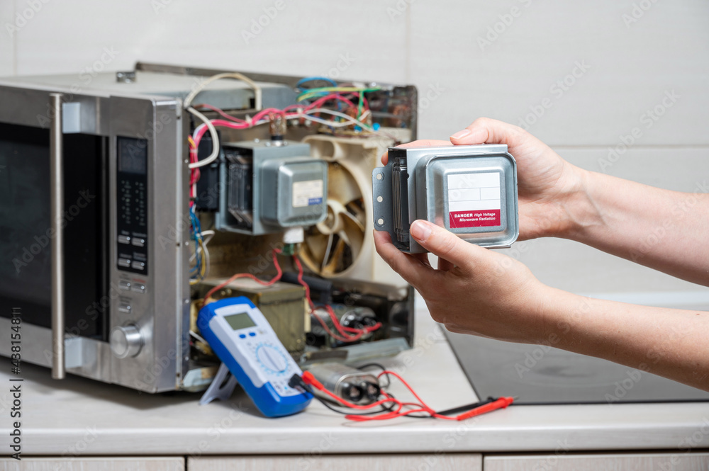 Repair of the microwave oven. The woman shows the new magnetron. Stock ...