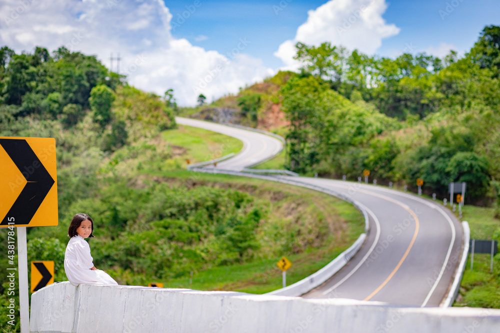 Little Asian girl in white dress sitting on road barrier with beautiful ...