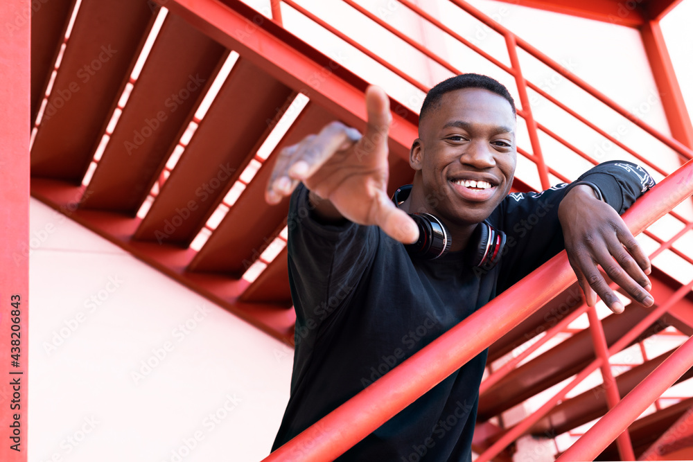 Joyful black man raising arm reaching out to camera on staircase Stock ...