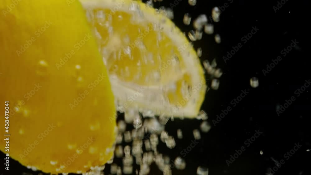 Close-up of falling sliced lemons into the sparkling water on black ...