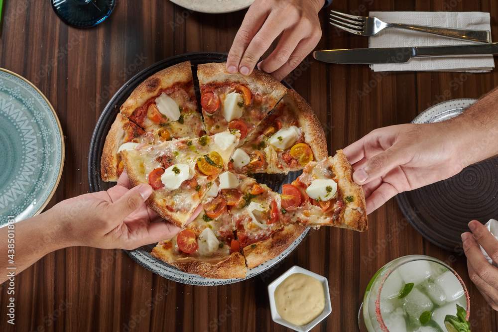 manos de hombres compartiendo una pizza de tomate sobre una mesa ...