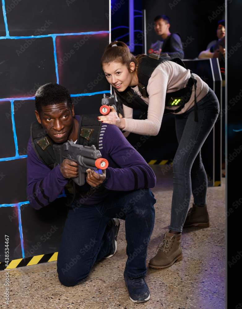 Young laser tag players of different nationalities aiming laser guns at ...