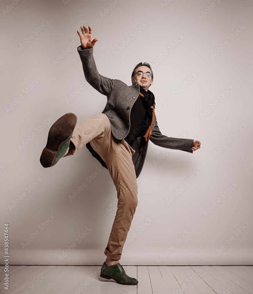 Stylish adult man hipster in pants and plaid jacket stands holding foot ...