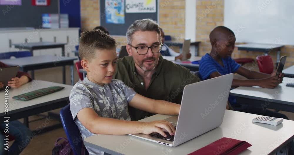 Diverse male teacher helping a schoolboy sitting in classroom using ...
