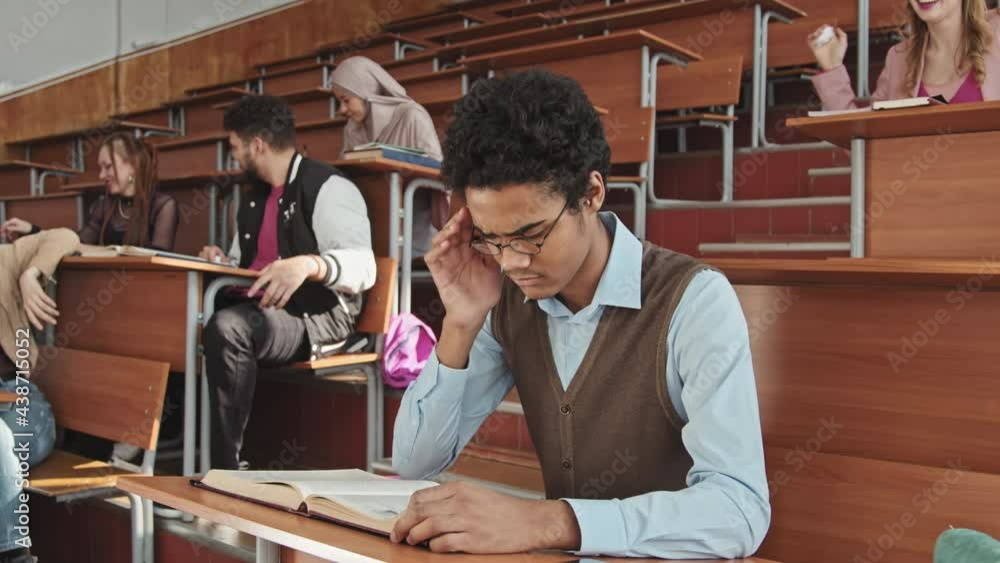 Medium slowmo of sad Mixed-race boy sitting alone in class while his ...