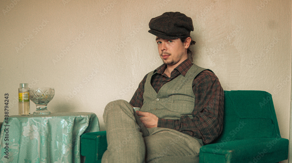 man in vintage suit is sitting on sofa and holding coffee cup. an old ...