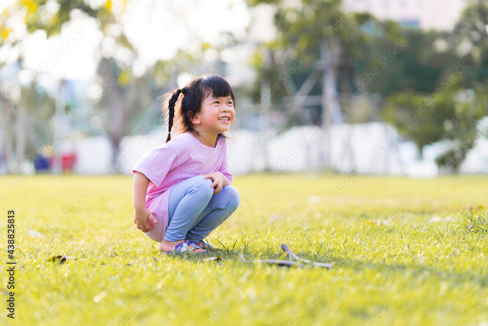 Asian girl squatting on the green lawn. Little child was scratching her ...