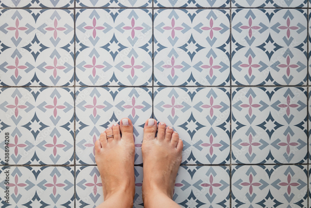 Young female bare feet with a ring on a toe on a light tile with a ...