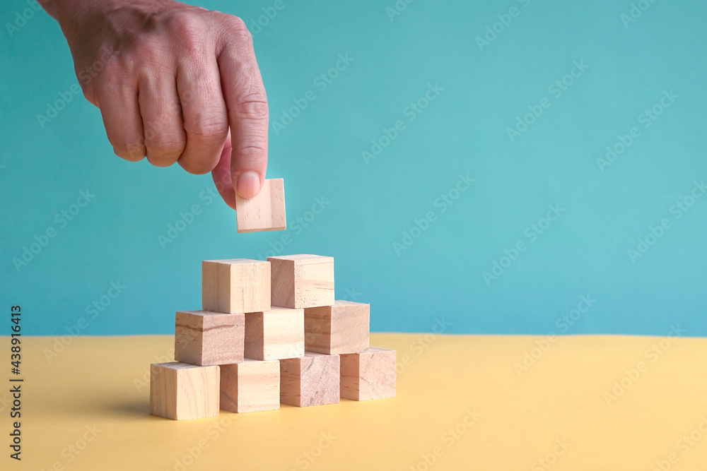 Hand putting a square wood block on pyramid stack of wood blocks. On ...
