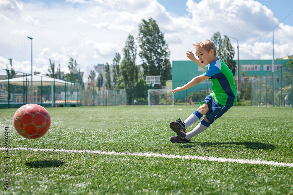 Little boy in blue and green form playing football on open field in the ...