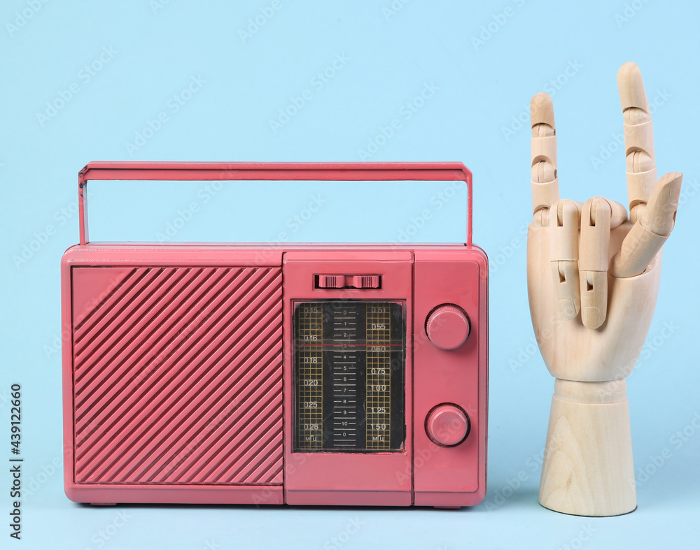 Pink retro radio receiver and wooden hand showing rock gesture on blue ...