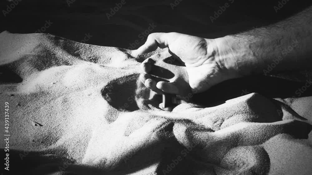 Black-and-white shot: the hand of a man grabbing sand, in the desert or ...