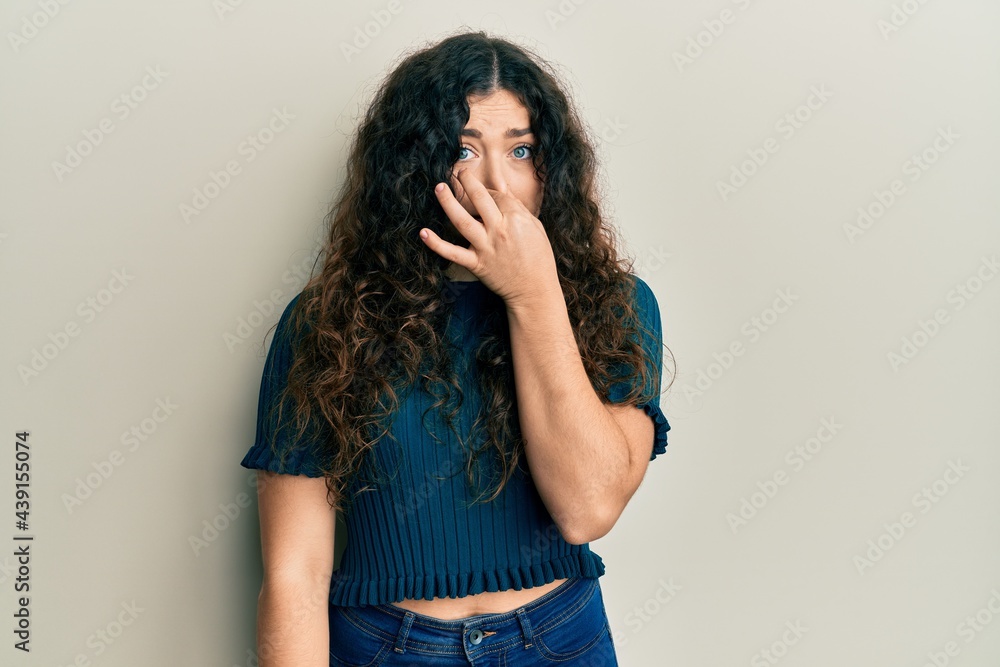 Young brunette woman with curly hair wearing casual clothes smelling ...