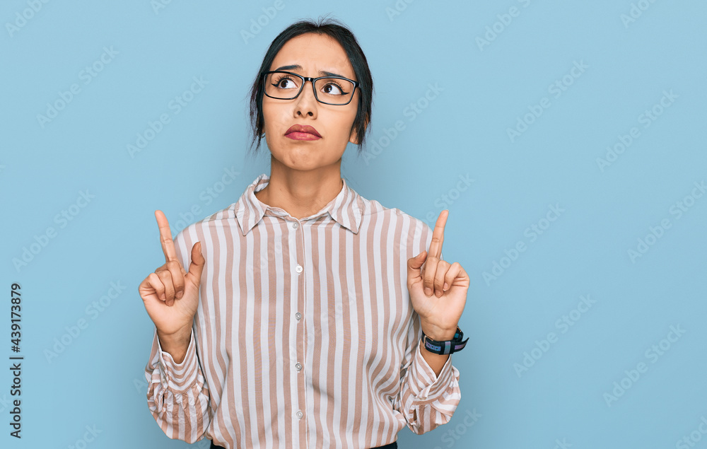 Young hispanic girl wearing casual clothes and glasses pointing up ...