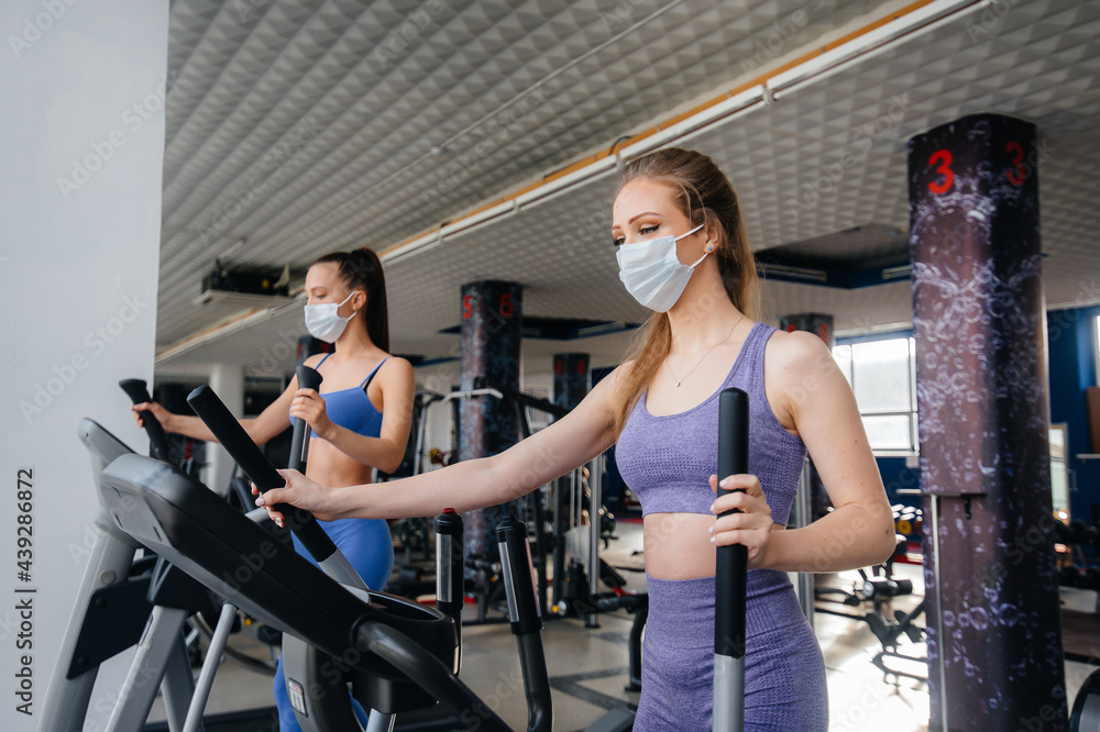 Two young beautiful girls exercise in the gym wearing masks during the ...